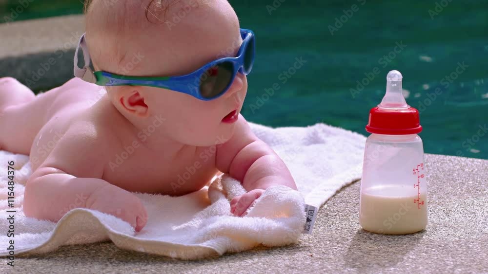 Cute baby boy with sunglasses, lying on a towel at the pools edge, with ...