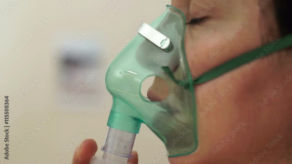 Close up side shot of a woman using a breathing mask nebulizer ...