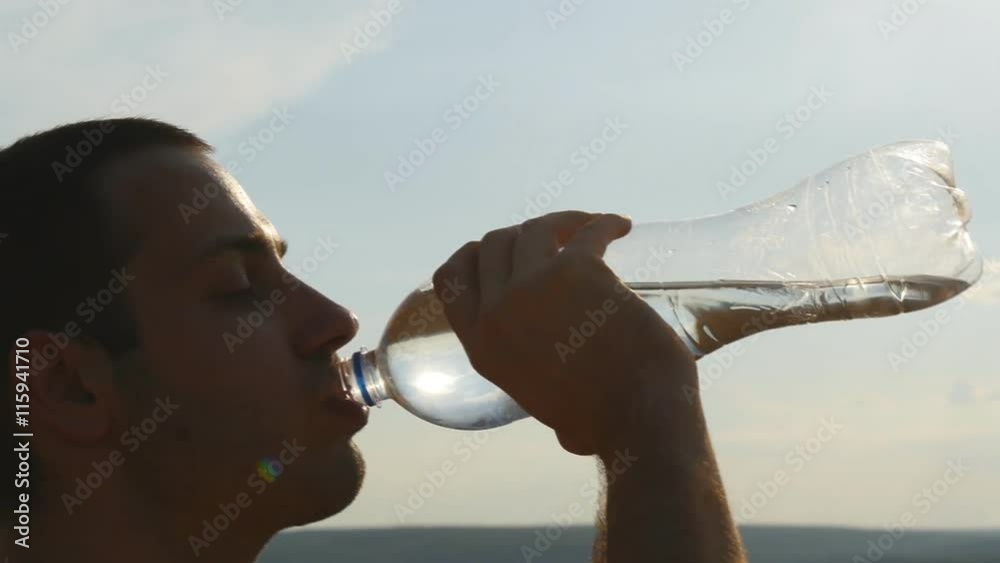 Young man drinking water from a plastic bottle in nature. Guy having ...