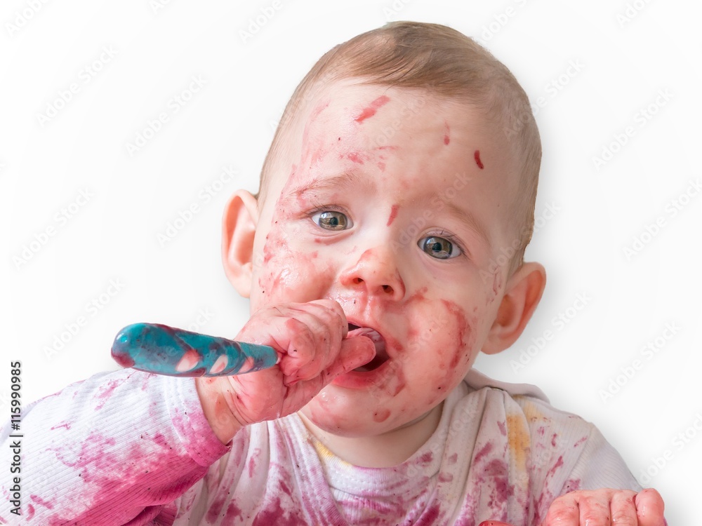Little messy and dirty baby is eating fruit snack and licking spoon ...