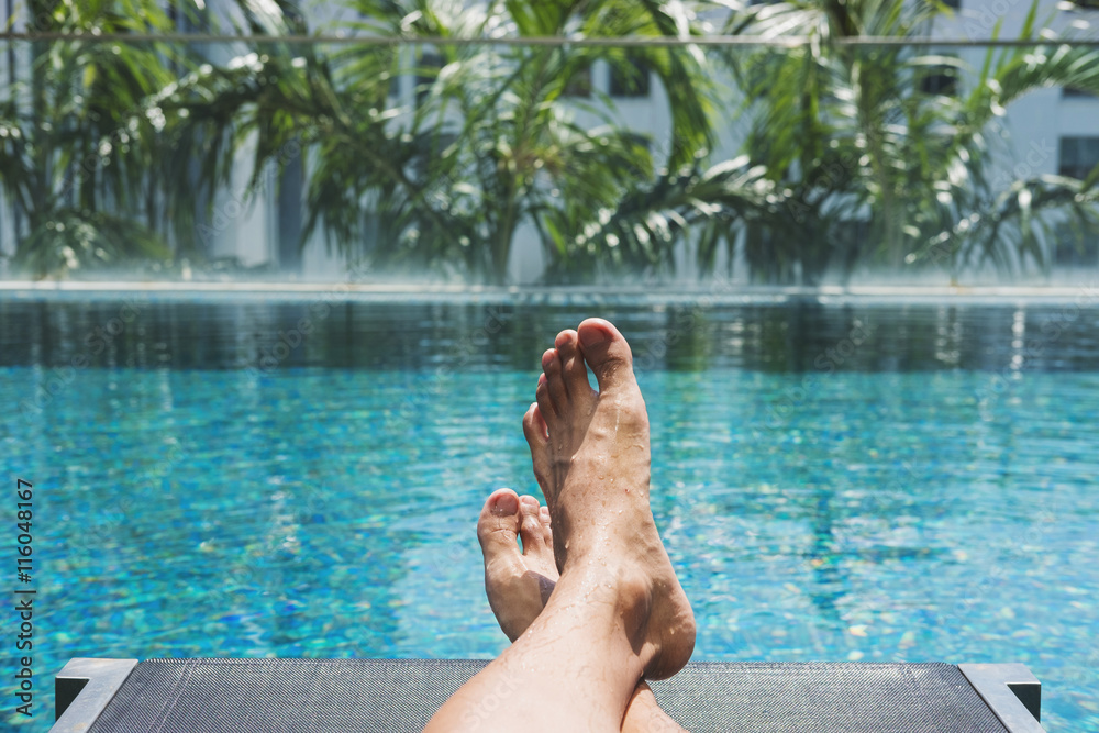 Sunbathing at swimming pool at tropical resort in summer, Asian guy feet lying down on ...