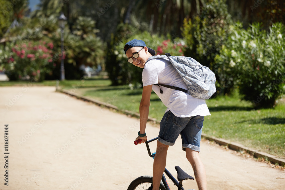 Rear view of young Caucasian BMX rider in street wear and glasses ...