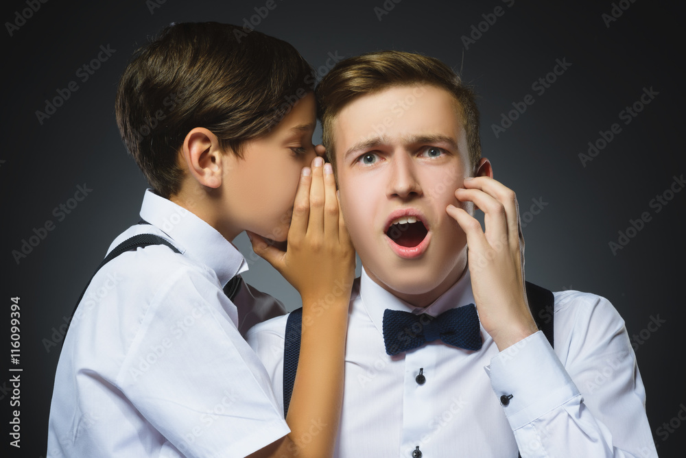 boy whispering in the ear of Teenager or brother on gray background ...
