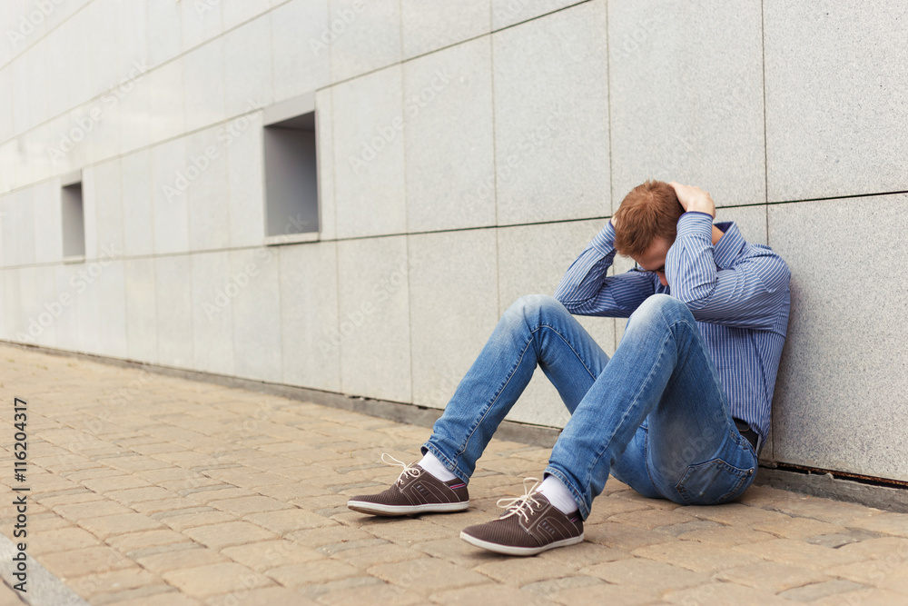 Portrait of young depressed desperate man sitting outdoor, holding his ...