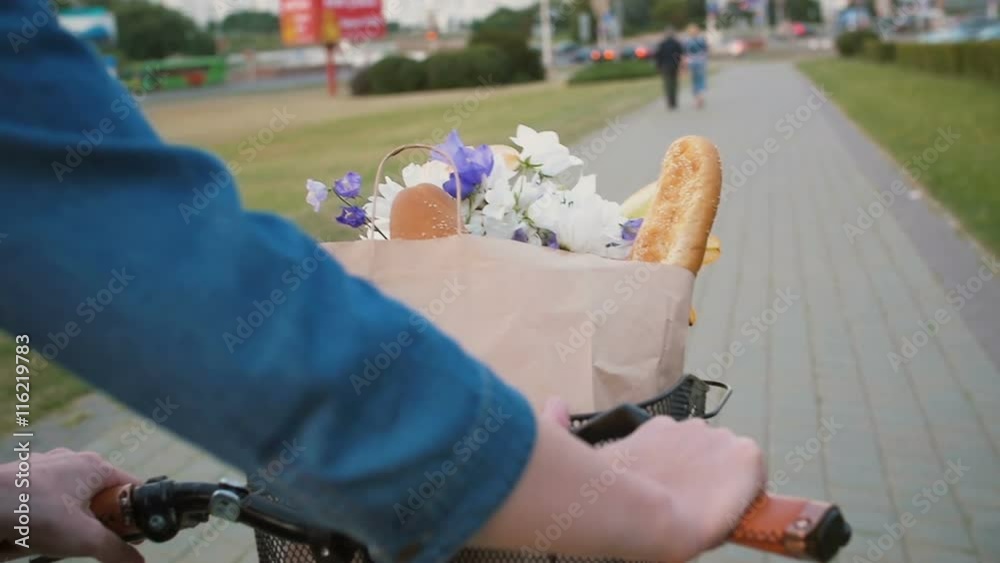 Woman hands on handlebar of bike with flowers and bread in basket as ...