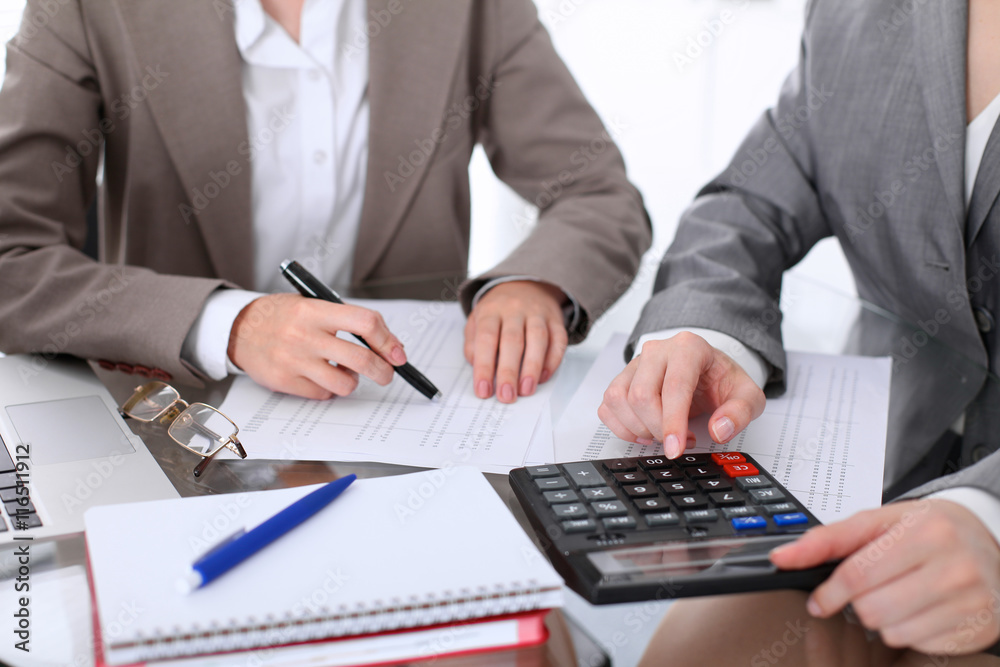 Two female accountants counting on calculator income for tax form ...