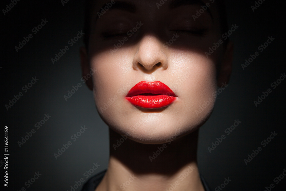 Beautiful model with bright red lips and face half covered in shadow ...