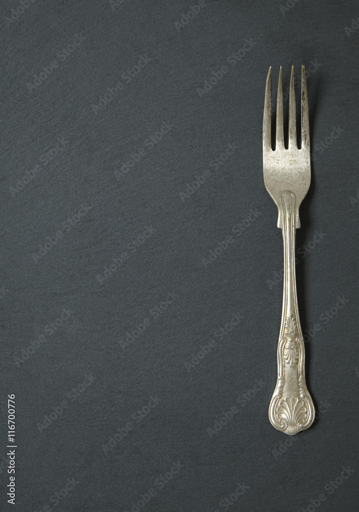 Antique style fork on a rustic slate background forming a page border ...