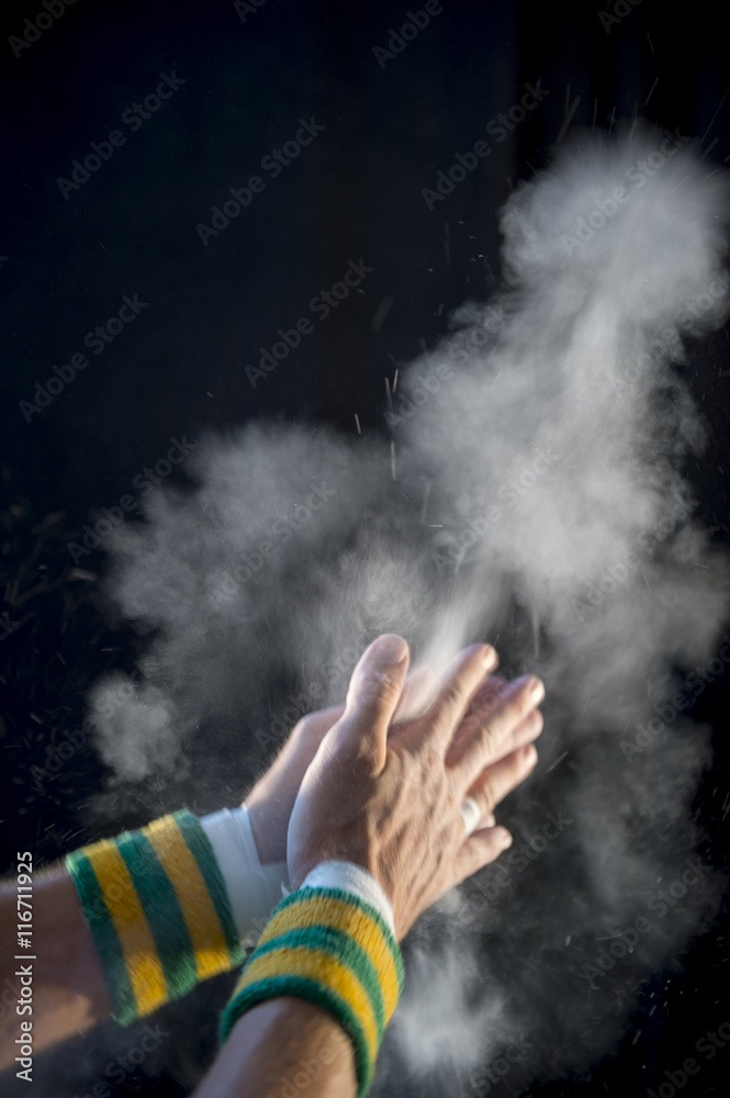Taped hands of gymnast clapping white chalk powder into a cloud against ...