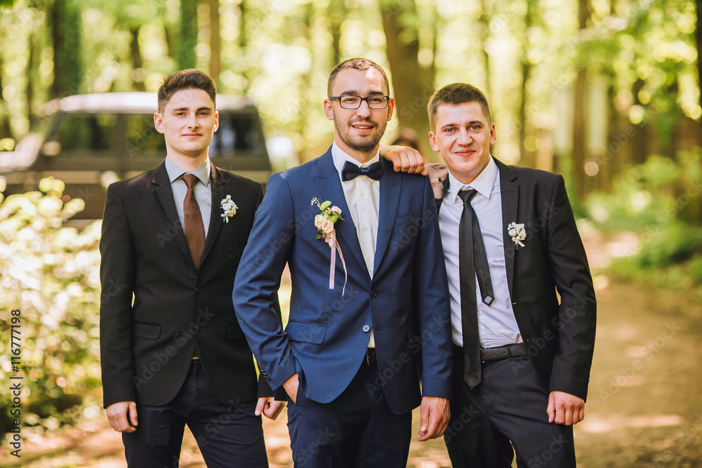 Confident smiling handsome groom in black suit with two groomsman in ...