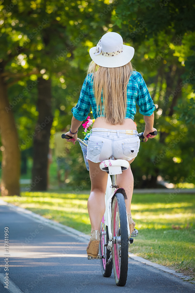 Back view of stylish young woman riding bicycle in a park. Fashion and ...