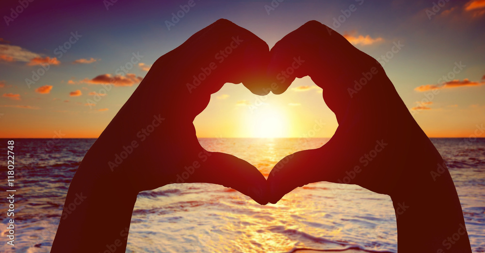 silhouette hands in heart shape with sunset in the middle and beach ...