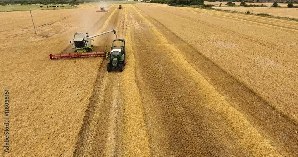 Aerial view flying over the top of a combine harvester and tractor and ...