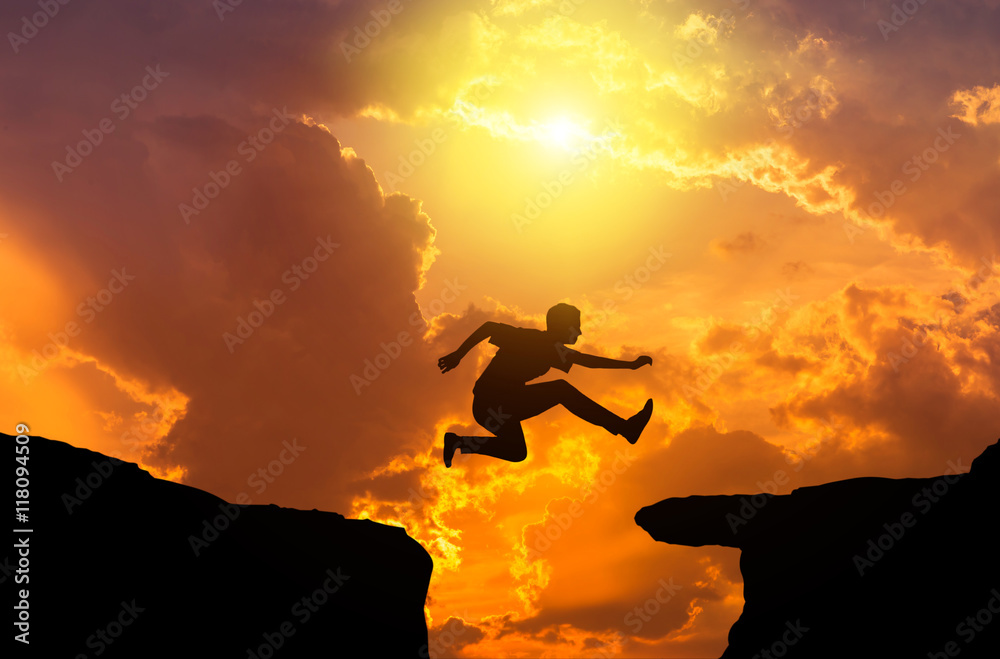silhouette the man jumping through the gap over rock cliff between ...