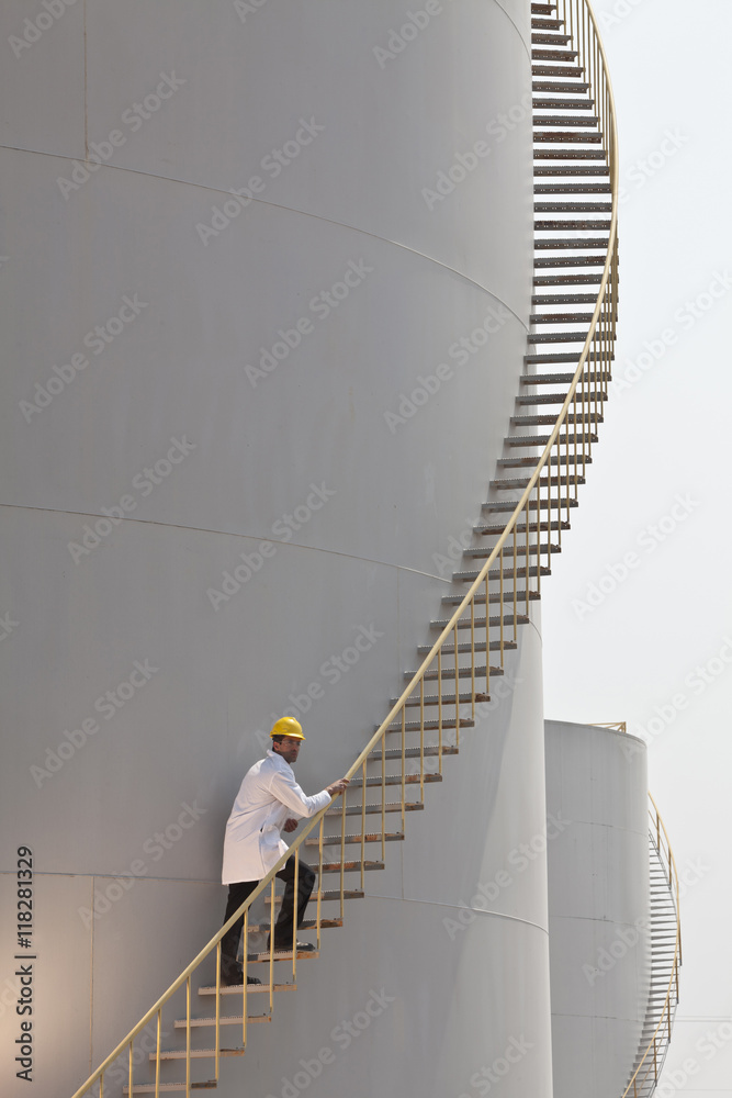 Caucasian worker climbing staircase on storage tank Stock Photo | Adobe ...