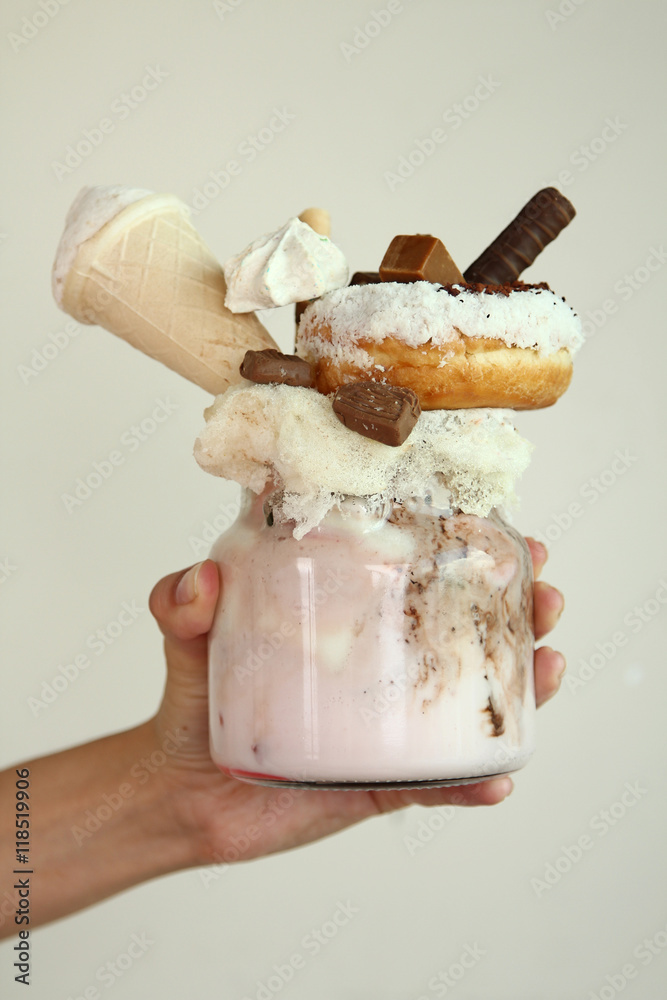 Female hand holding a milkshake, doughnuts and other sweets in a jar ...