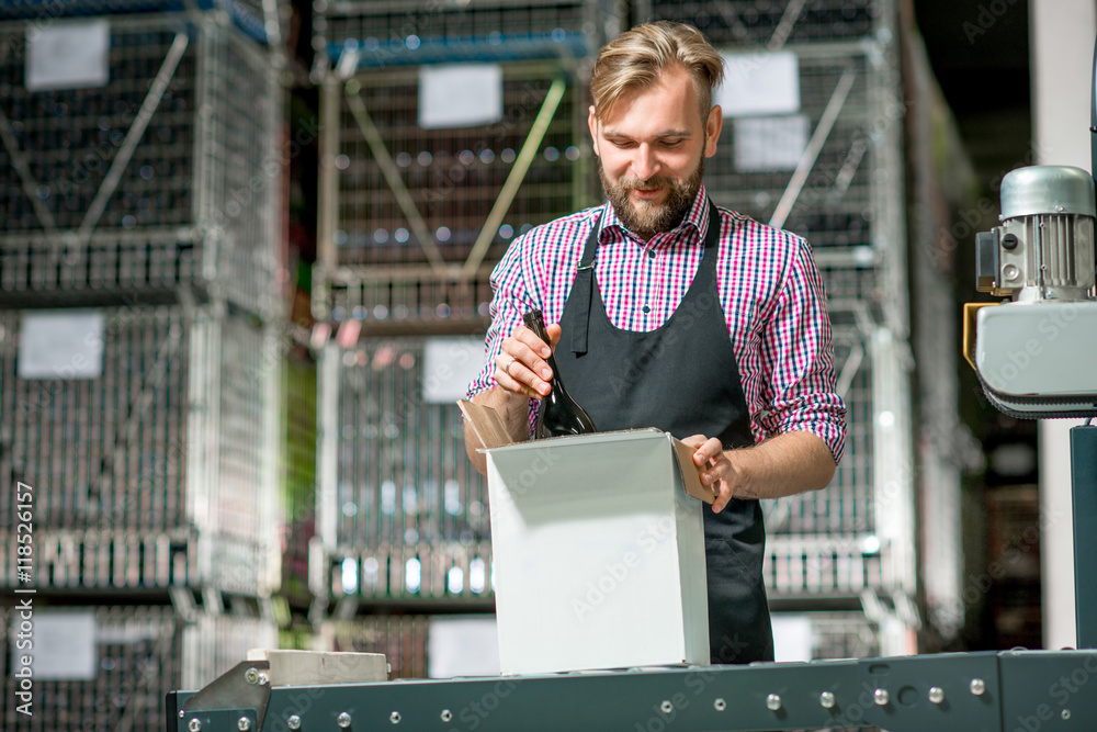 Handsome packer in working apron with box on the packaging line at the ...