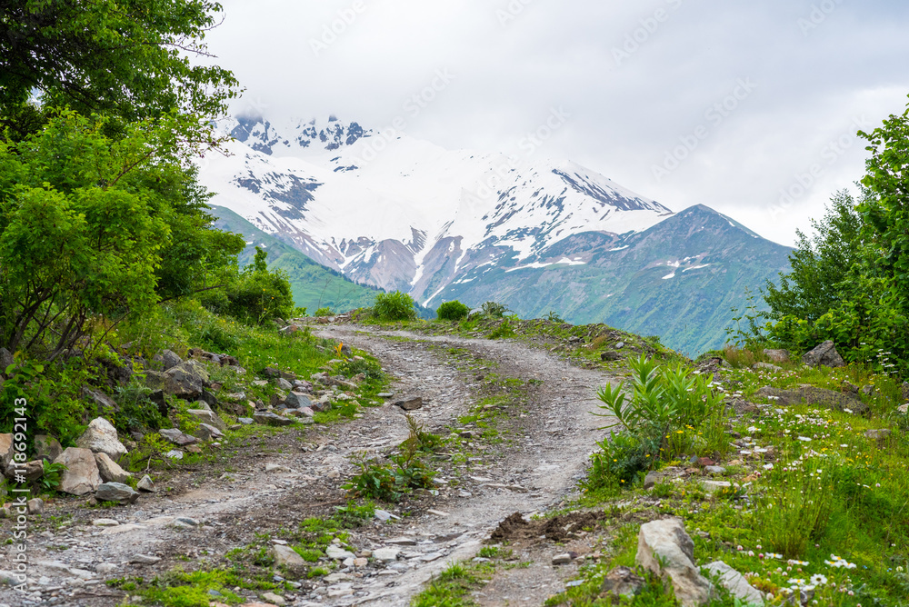 Stony dirt road in mountains with a view of snowy mountain in the ...