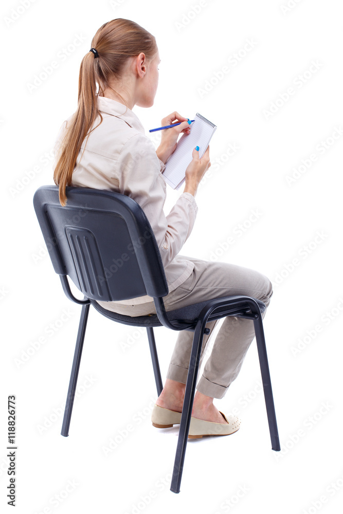 back view of young beautiful woman sitting on chair and takes notes in ...