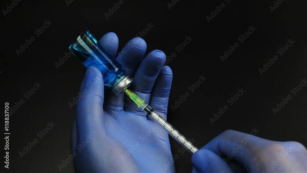 Syringe needle pierces the rubber stopper of the glass vial and filling ...