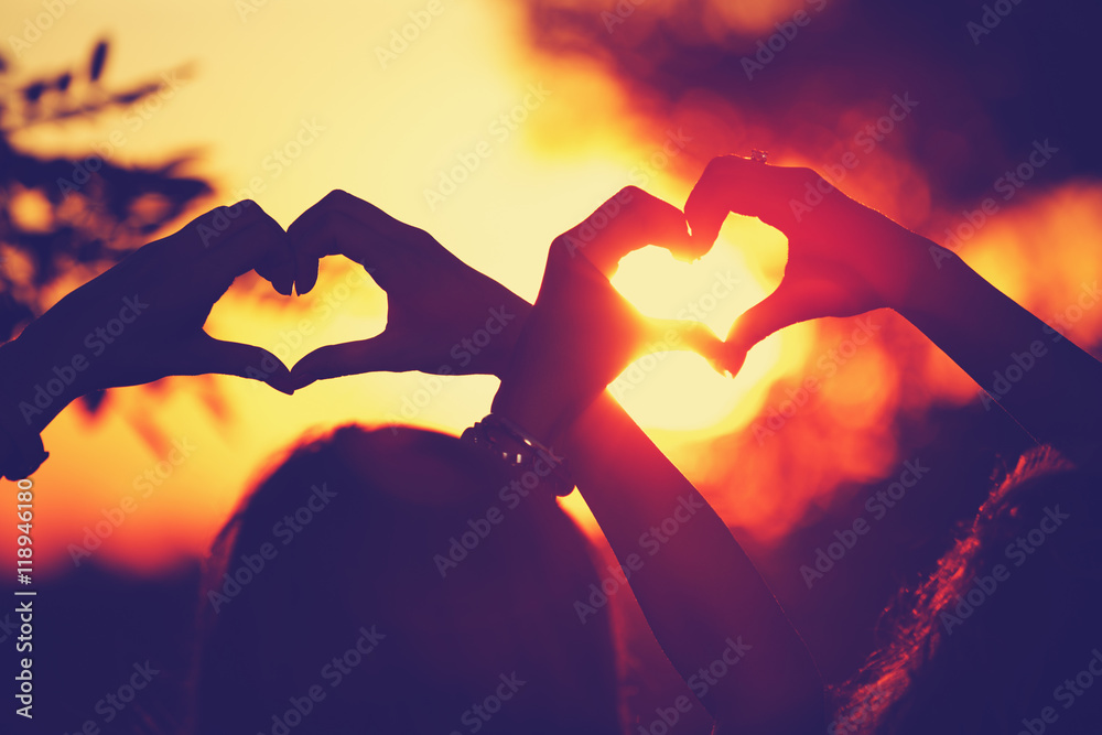 Girl-friends making a heart-shape for the sunset. Shallow depth of ...