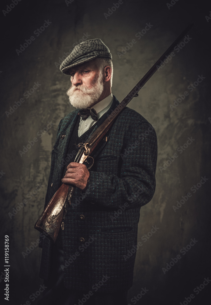 Senior hunter with a shotgun in a traditional shooting clothing, posing ...