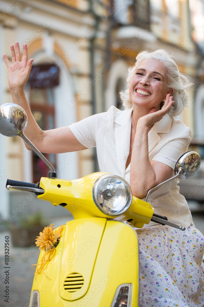 Mature lady waves hand. Lady on scooter is smiling. Meet old friends on ...
