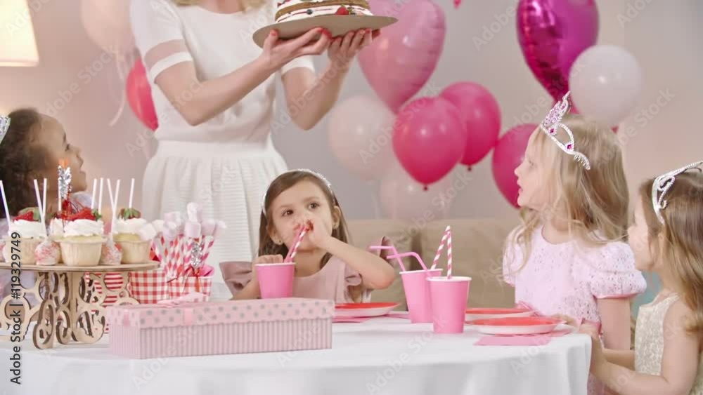 Mother putting birthday cake on table and little girls dressed like ...