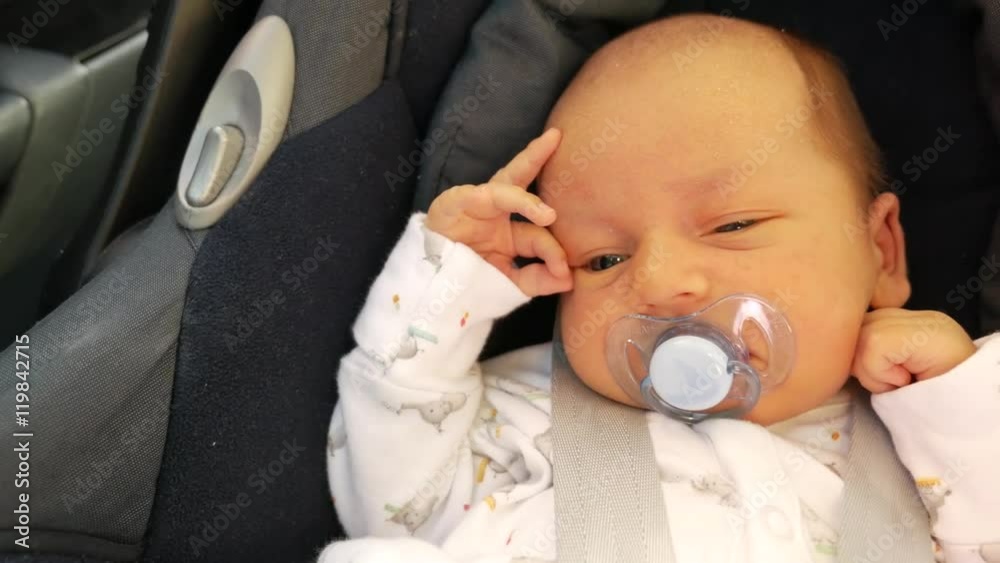 Calm drowsy baby in a child safety seat inside the car. Bany sucking ...