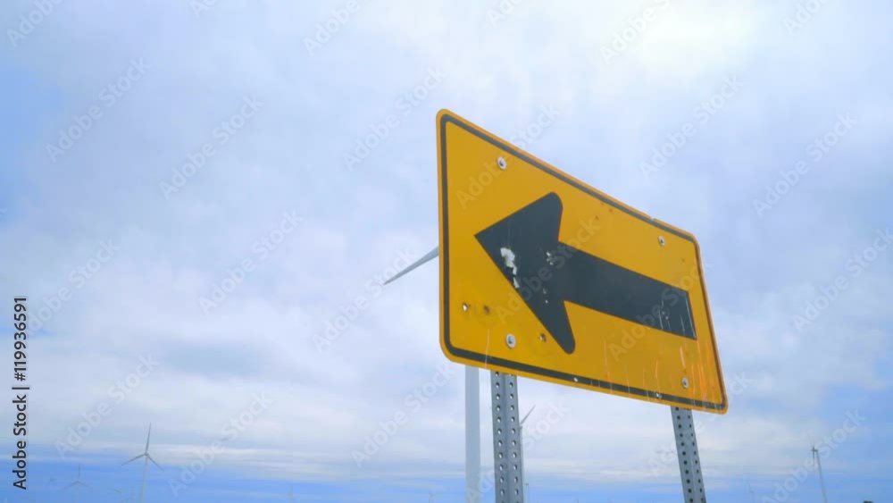 Road sign pointing to wing turbines field against clouds sky. Wind ...