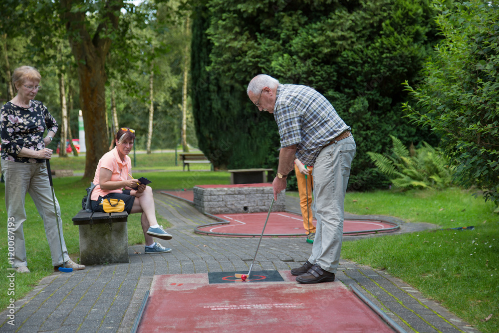 Senioren beim Minigolf. Der Mann steht konzentriert am Abschlag und ...