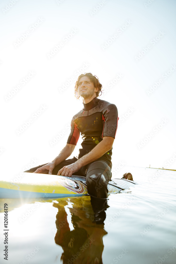 Handsome young surfer man in swimwear sitting on surf board Stock Photo ...