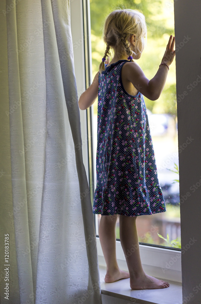 Little girl standing on window sill looking through window Stock Photo ...