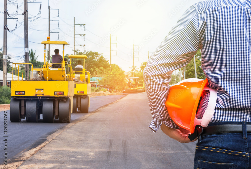 engineer holding safety helmet at road construction site with roller ...
