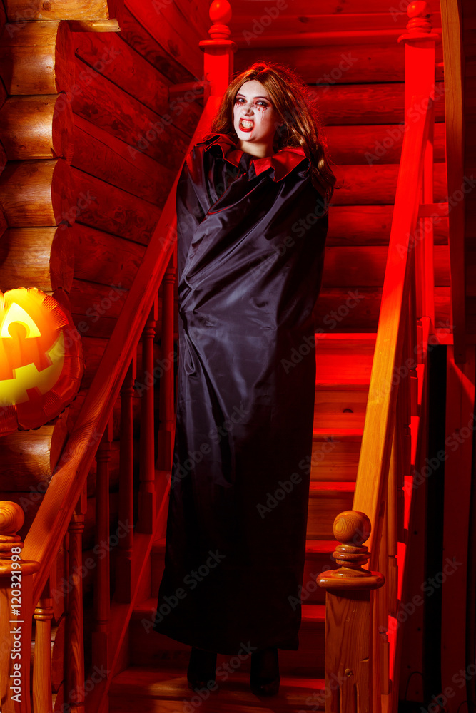 Vampire woman in cloak is standing indoors at stairs Stock Photo ...
