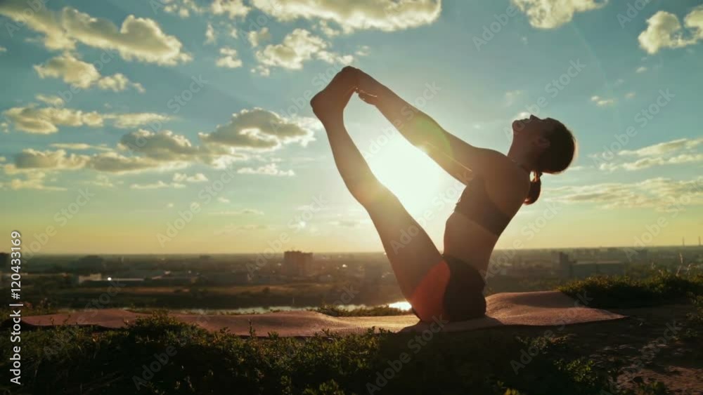 Silhouette of sporty woman doing yoga in floating boat pose in the park ...