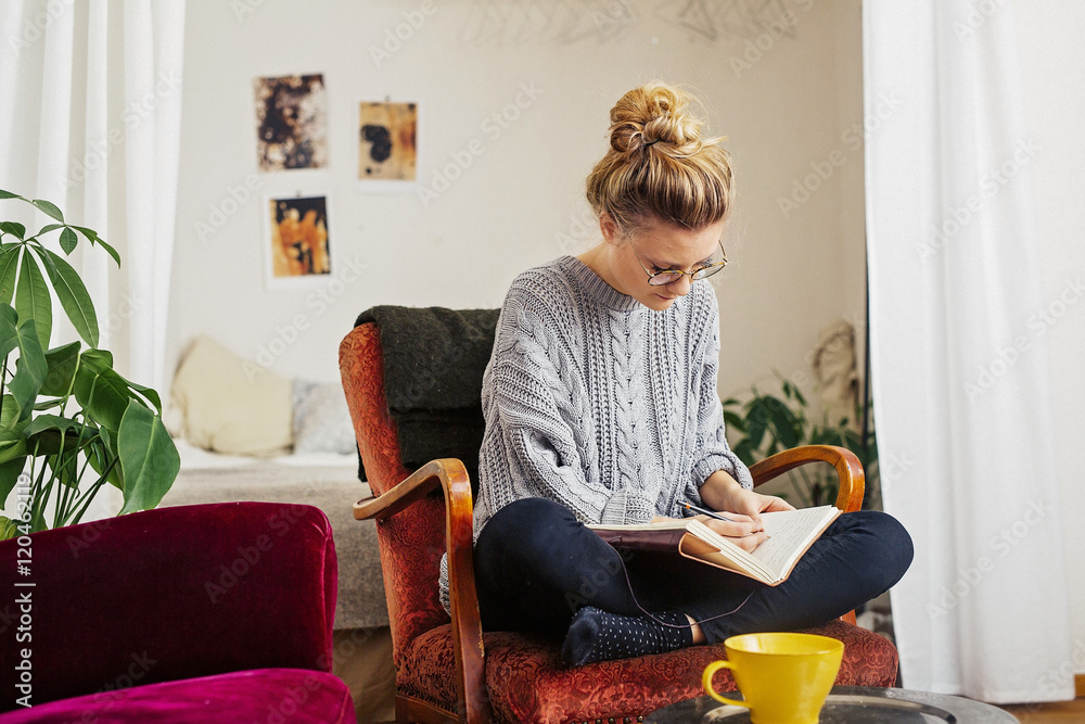 Woman writing on book while sitting on chair at home Stock Photo ...