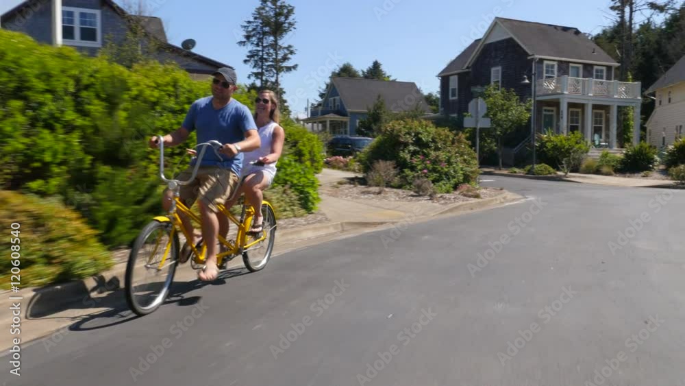 Couple riding tandem bicycle together in coastal vacation community ...