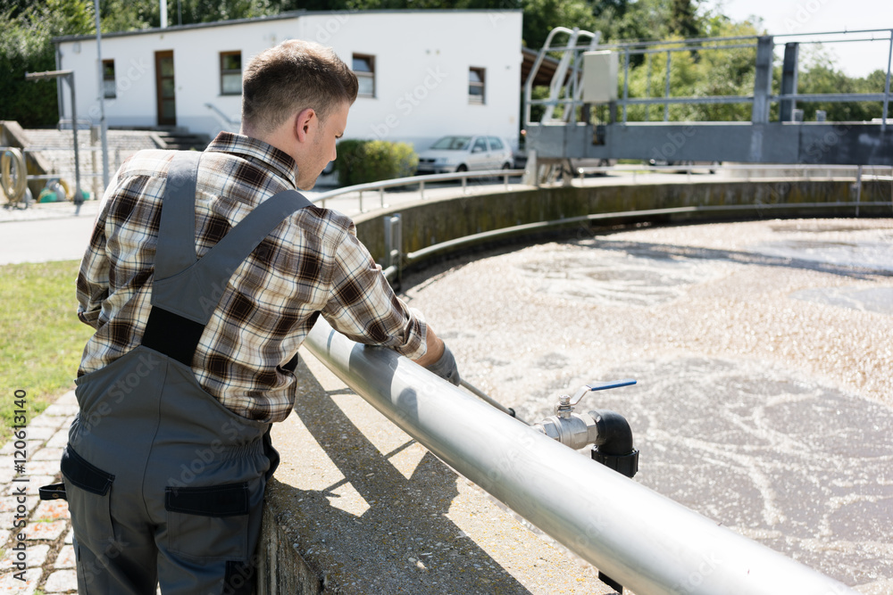 Worker taking water sample out of clarifier tank of sewage treatment ...