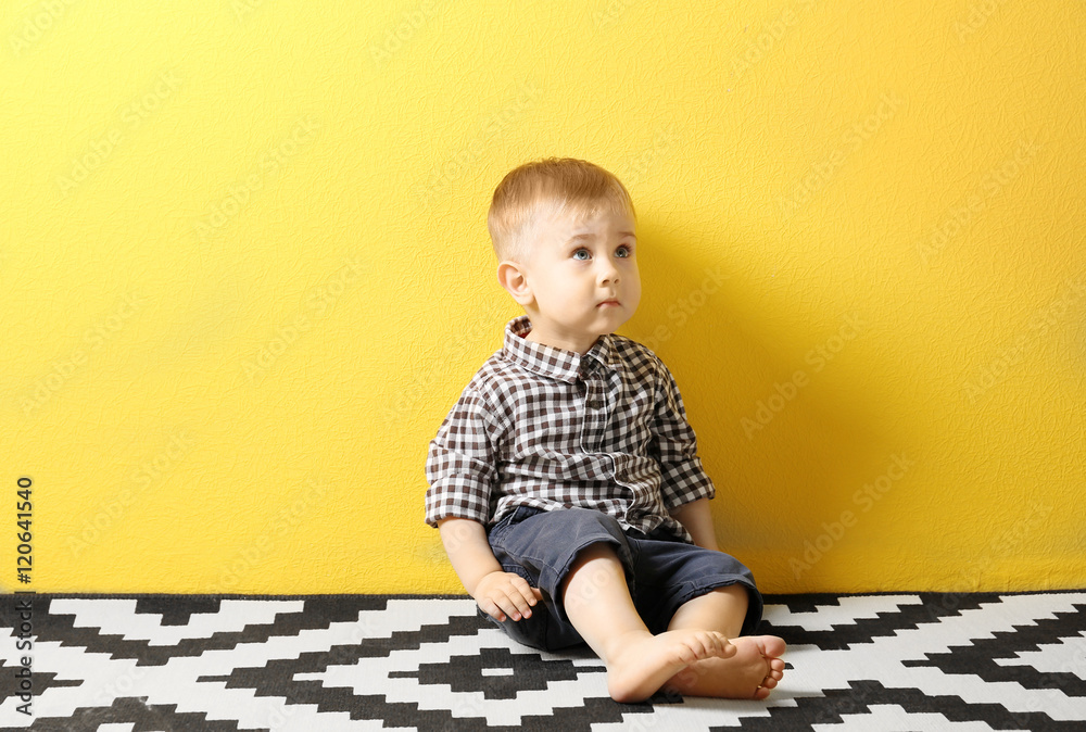 Stylish little boy sitting on the carpet with a pattern on a yellow ...