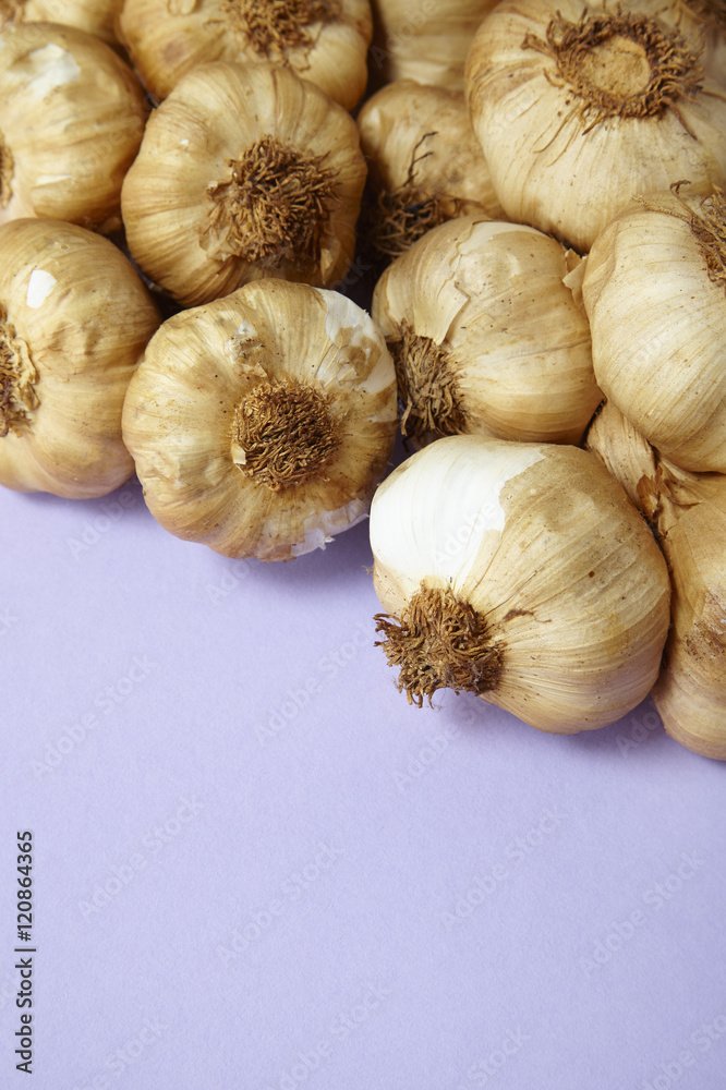 Bulbs of smoked garlic arranged on a pastel purple background to form a ...