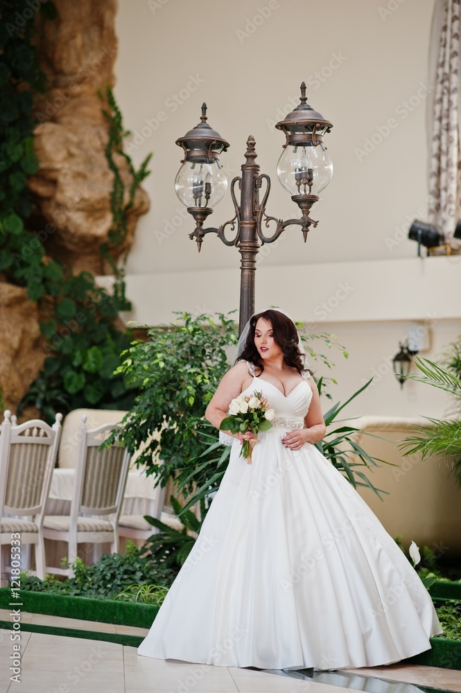 Big breasts brunette bride with wedding bouquet posed at wedding hall ...