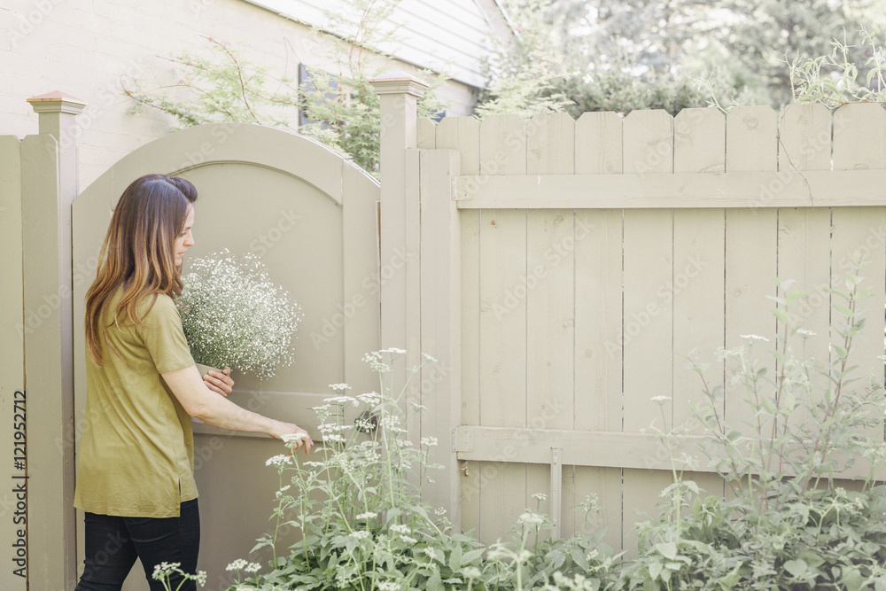 Woman entering a garden through a gate, carrying a bunch of white ...