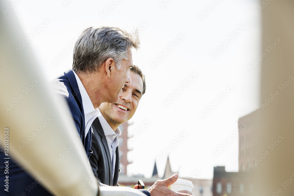 Two people, men talking together outdoors leaning on a railing, taking ...