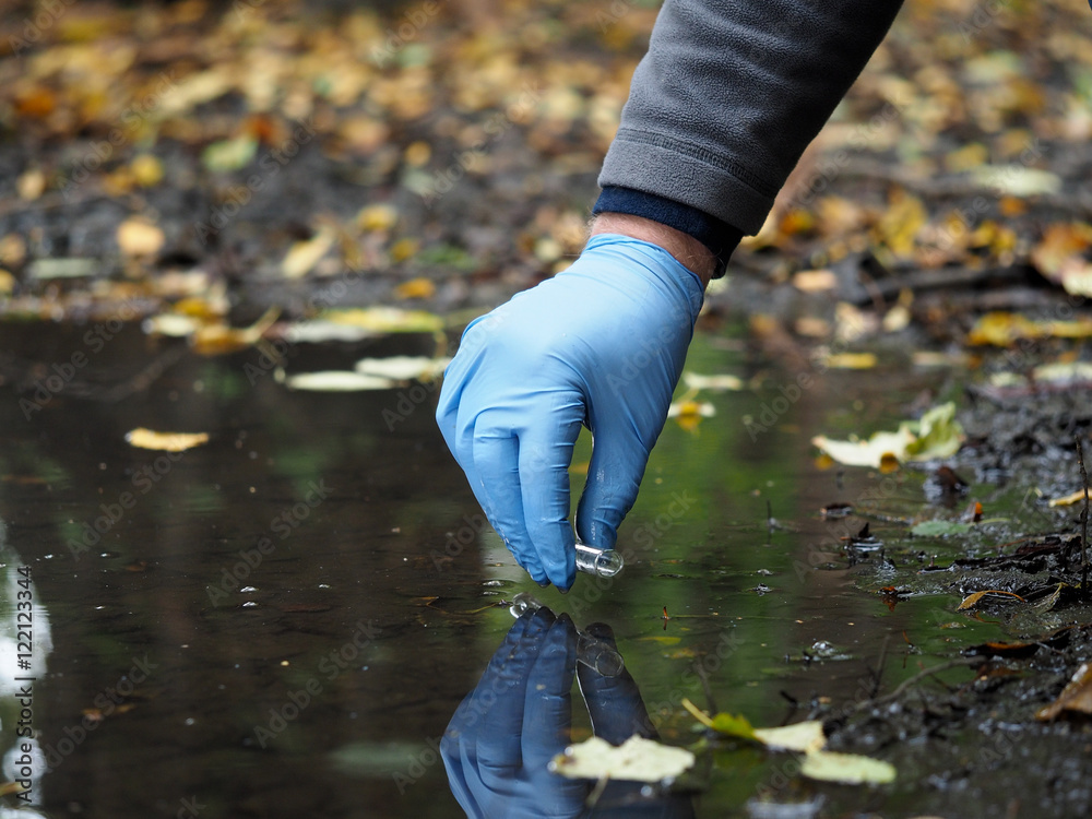 Water sample. Hand in glove collects water from a puddle in a test tube ...