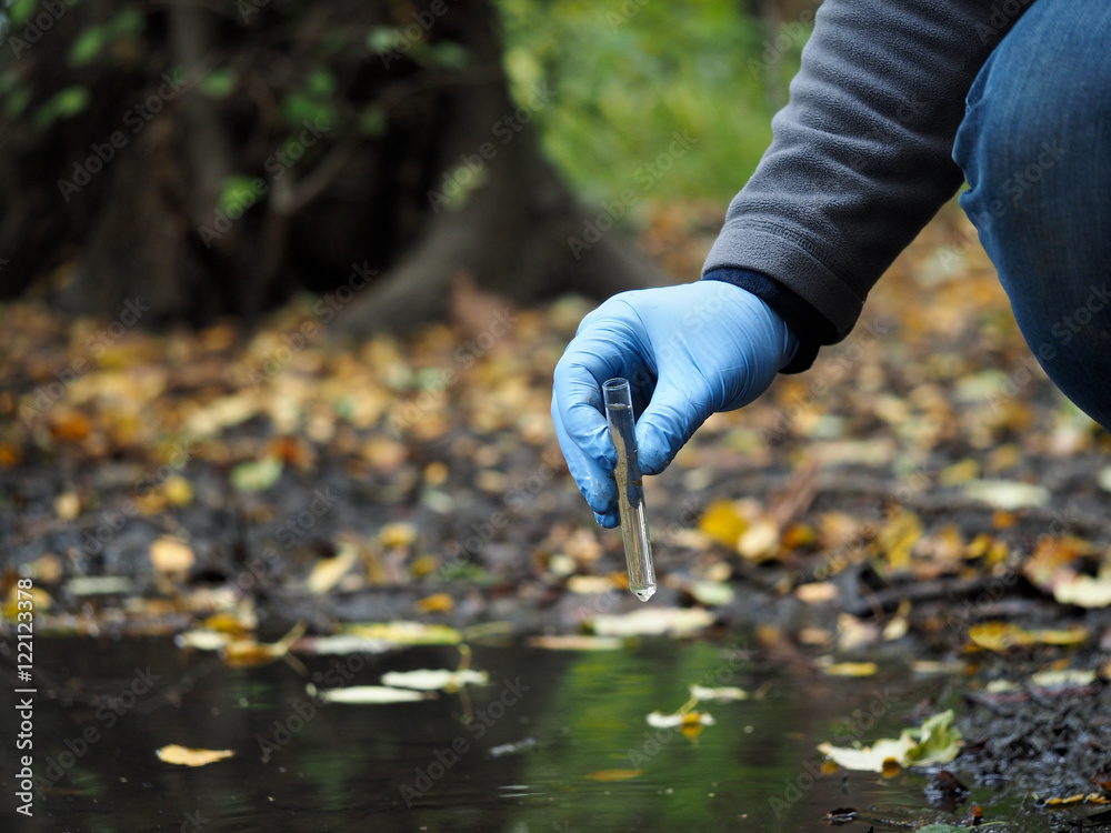 Water sample. Hand in glove collects water from a puddle in a test tube ...
