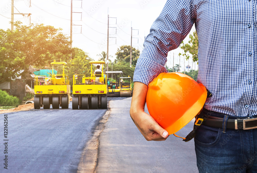 engineer holding safety helmet at road construction site with roller ...