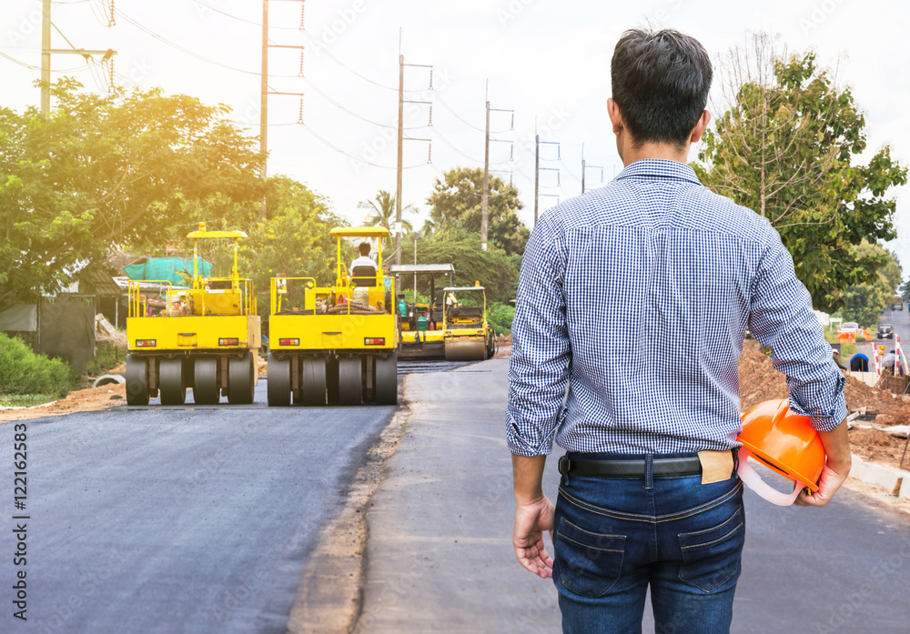 engineer holding safety helmet at road construction site with roller ...