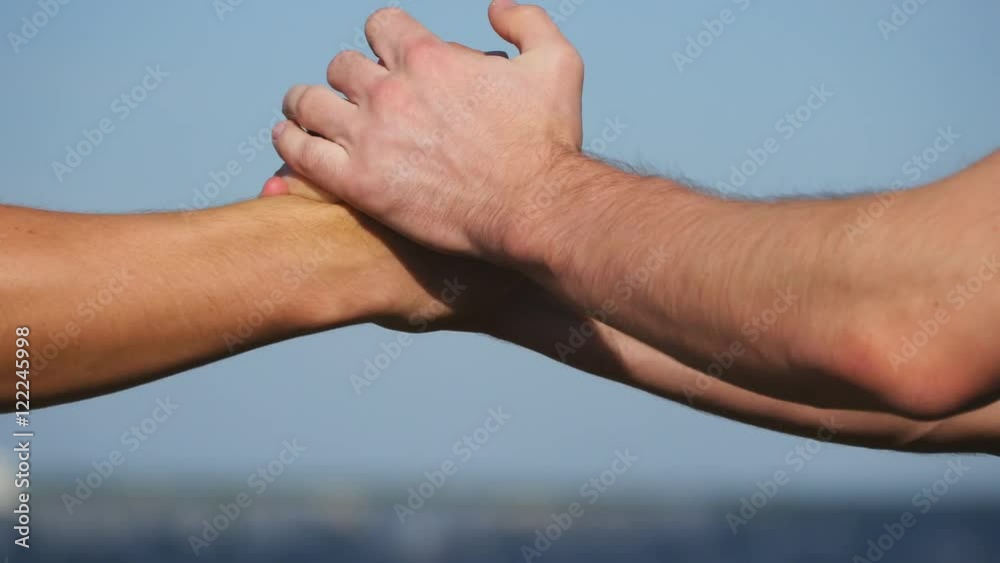 Friendly handshake of two unrecognizable muscular white men on blue sky ...