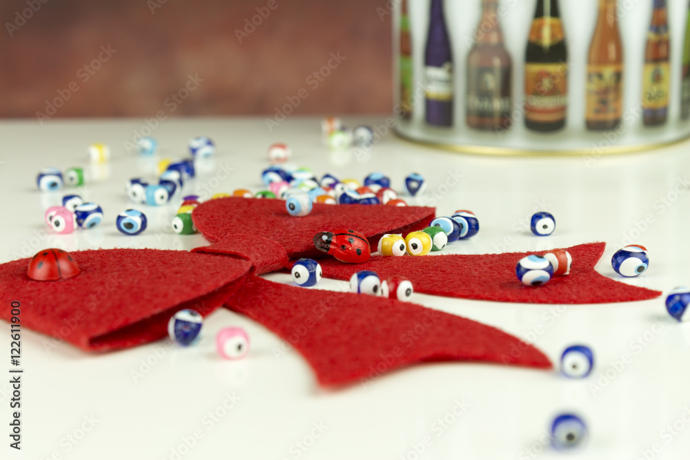 Vertical capture of red ribbon, lady bug and tiny evil eye beads on ...